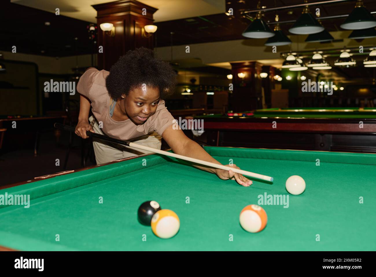 Young active woman in casual attire bending over pool table and looking ...