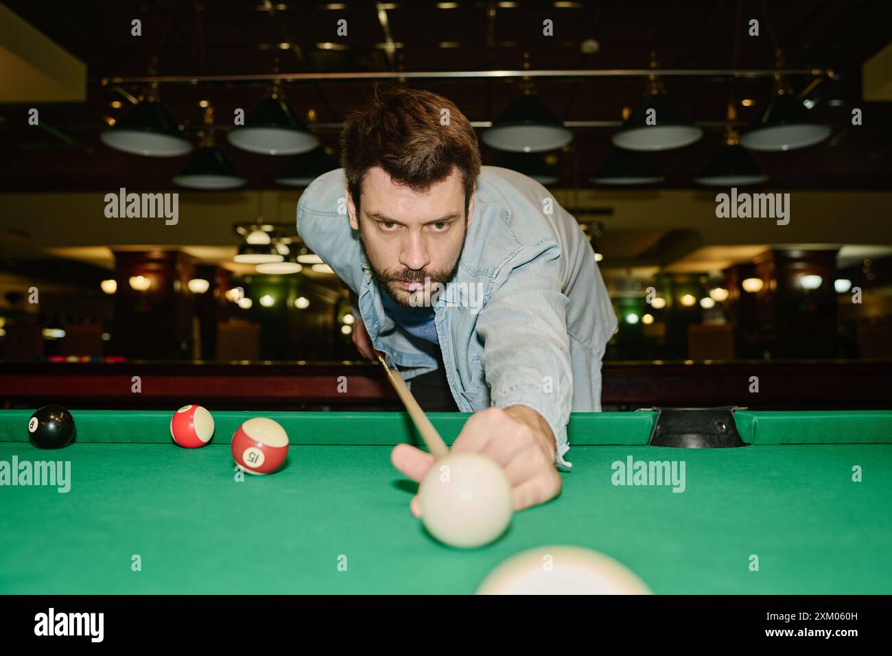 Young serious man in casualwear looking at pool ball and hitting it ...