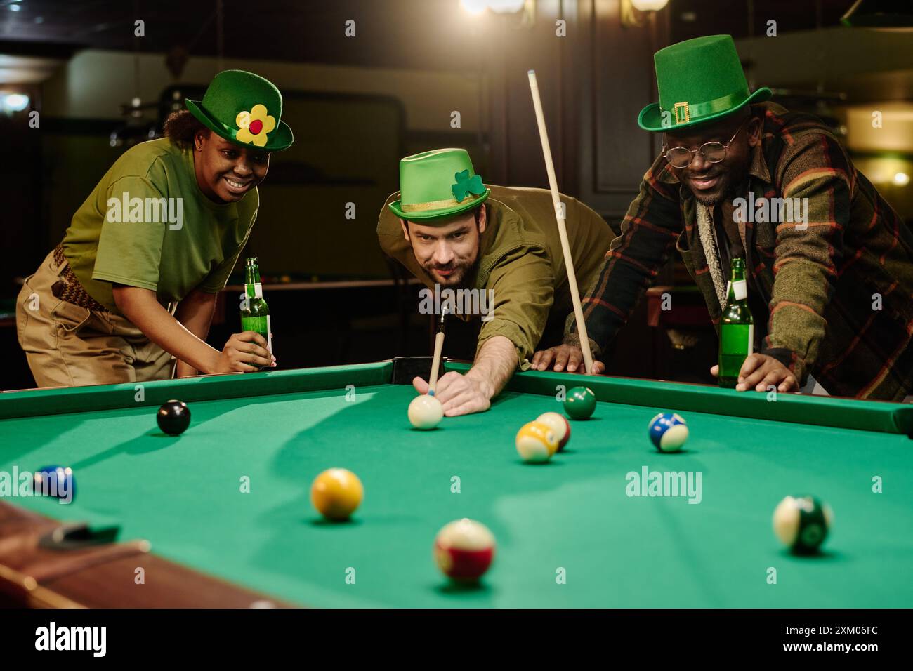 Three happy young friends in green hats having beer and enjoying ...