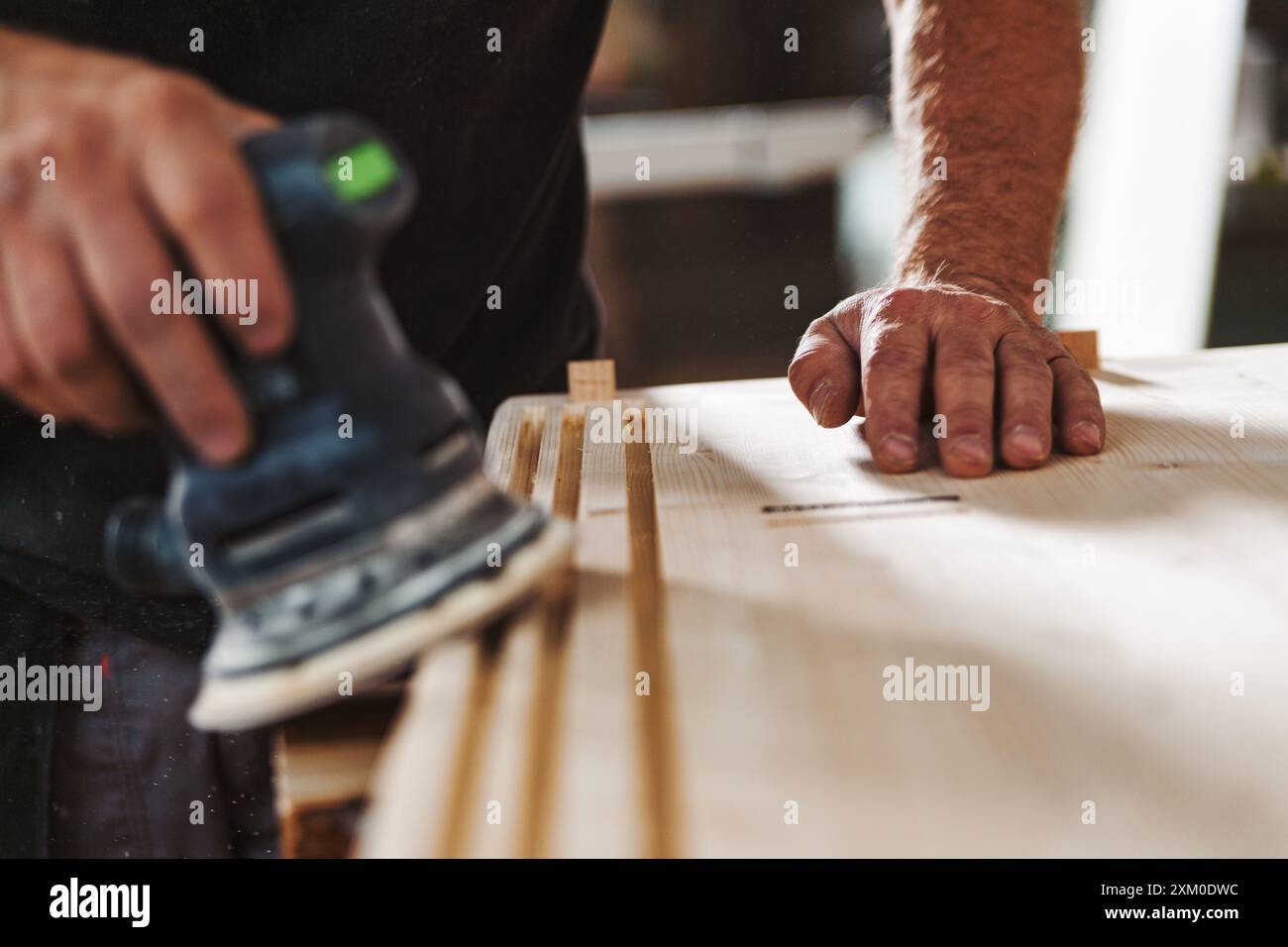 Skilled carpenter sanding wood with electric sander in workshop ...
