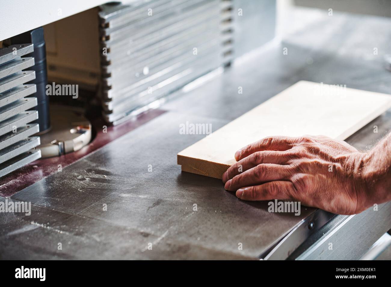 Carpenter is smoothing a plank of wood using a surface planer in a ...