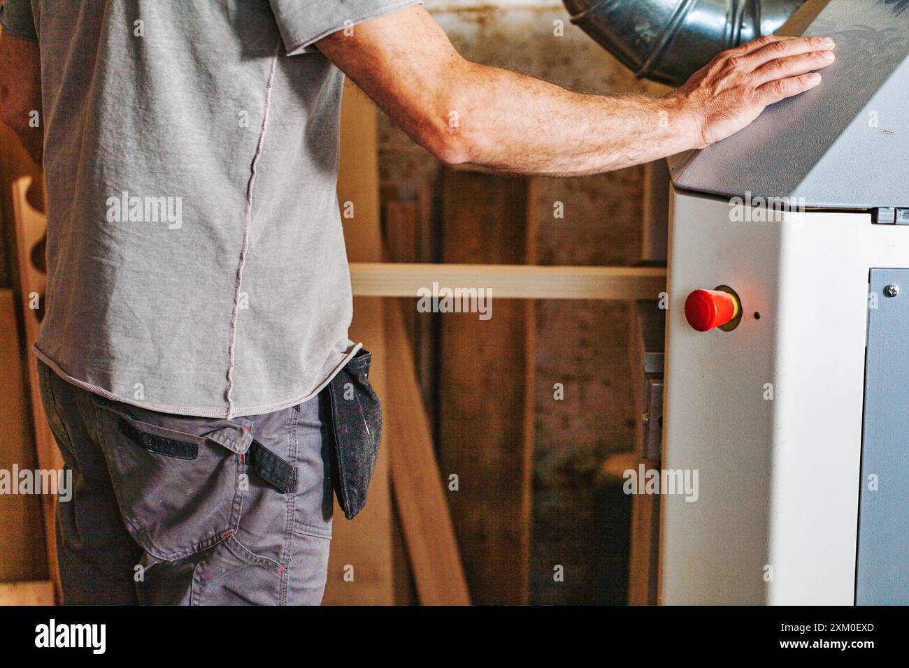 Carpenter is using a thickness planer in his workshop. He is wearing a ...