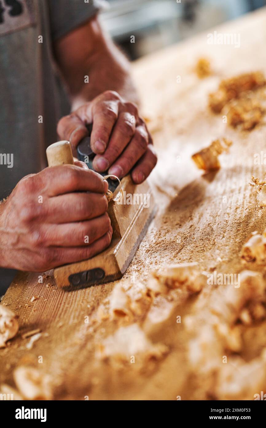 Skilled carpenter smoothing wood with hand plane in workshop, revealing ...