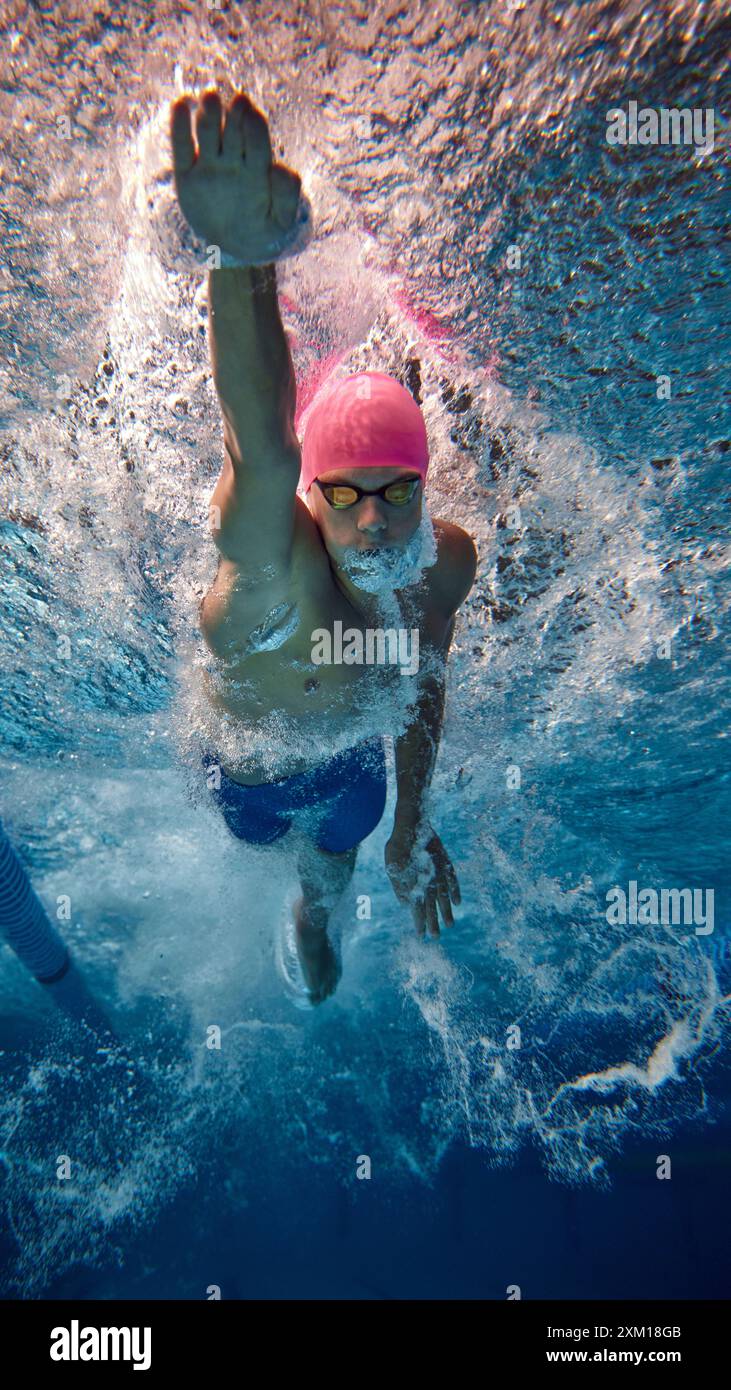 Athletic male swimmer captured mid-freestyle stroke underwater, displaying strength and ...