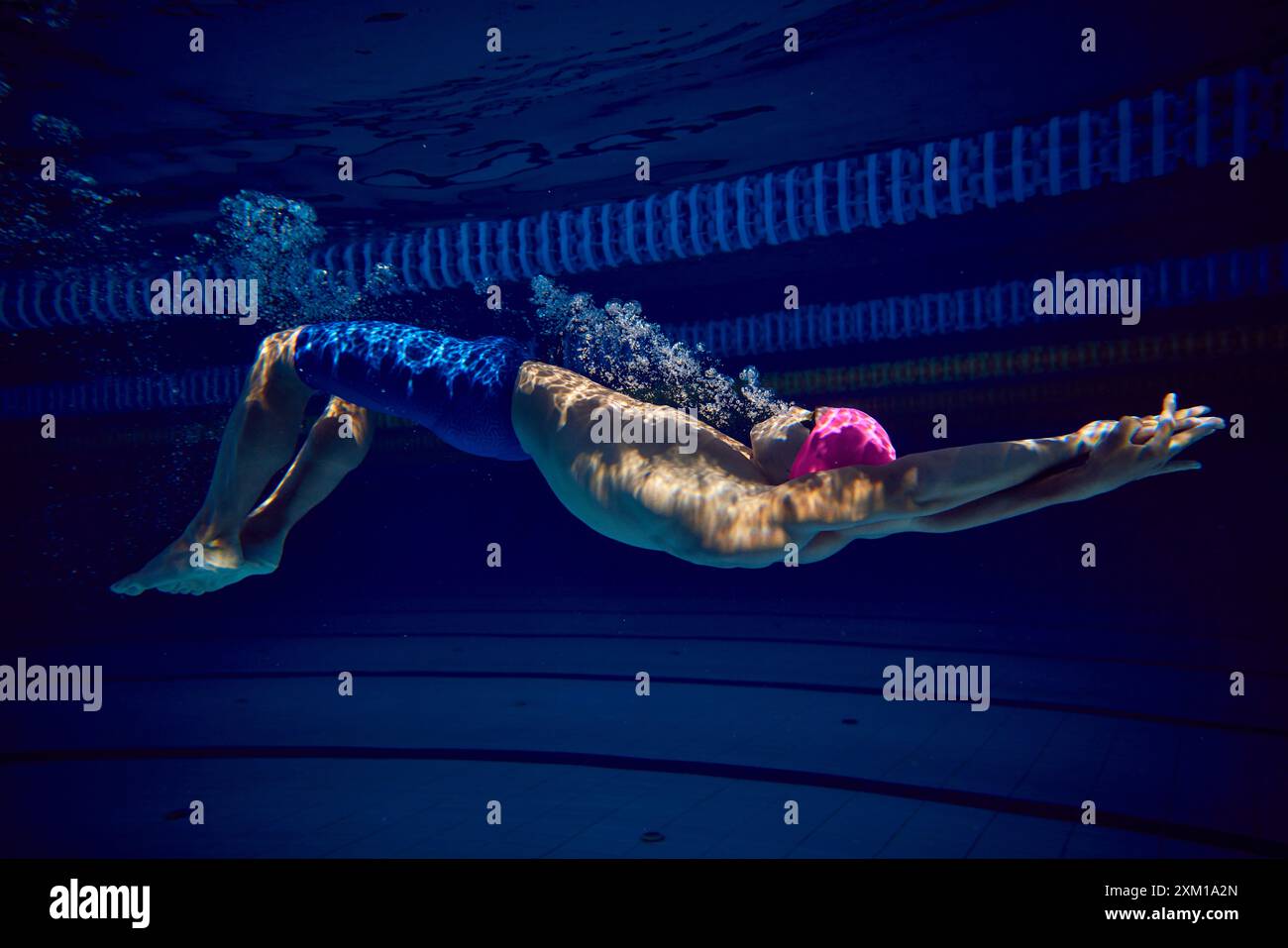 Male swimmer, wearing pink cap and blue trunks, in training shows his ...