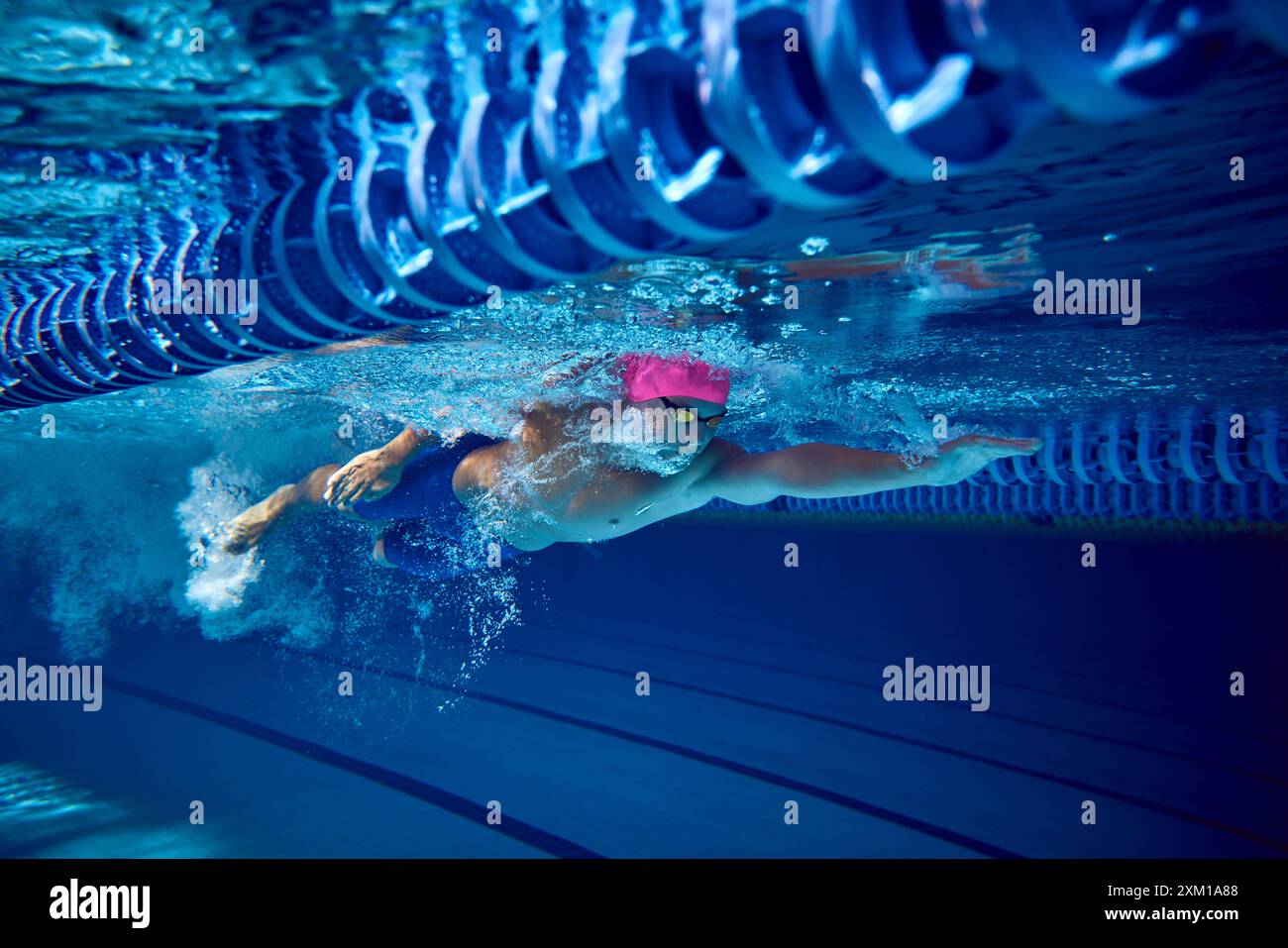 Competitive swimmer, with pink cap and blue trunks, seen underwater ...