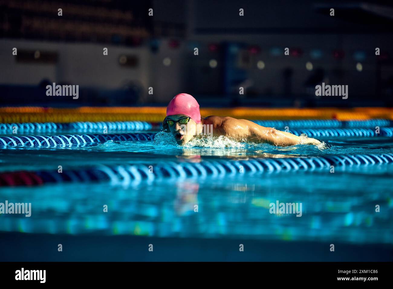 Athlete in pink cap and goggles executes butterfly stroke, his muscular ...