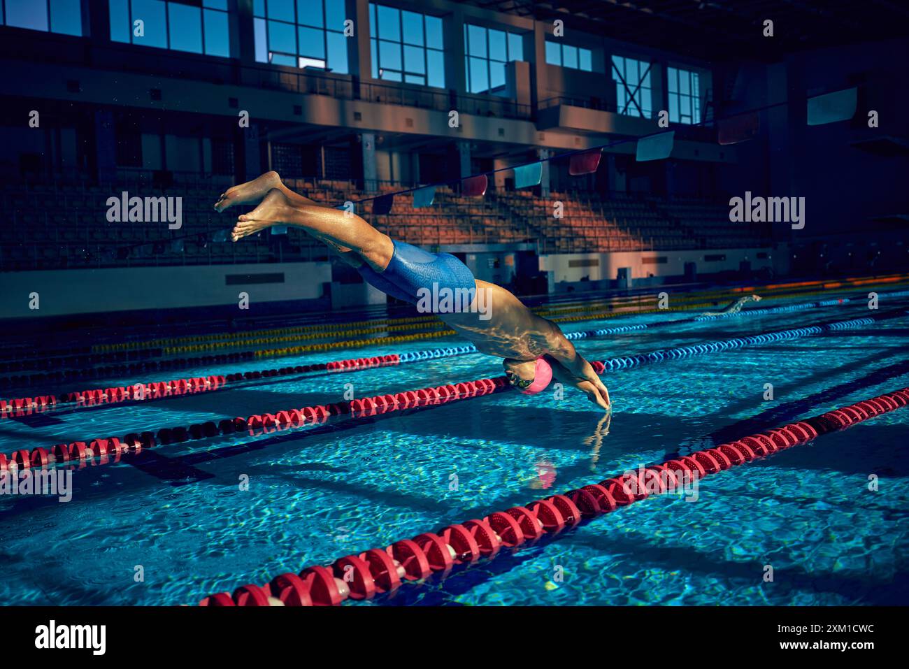 Dynamic photo of athlete wearing pink swim cap and blue trunks dives ...