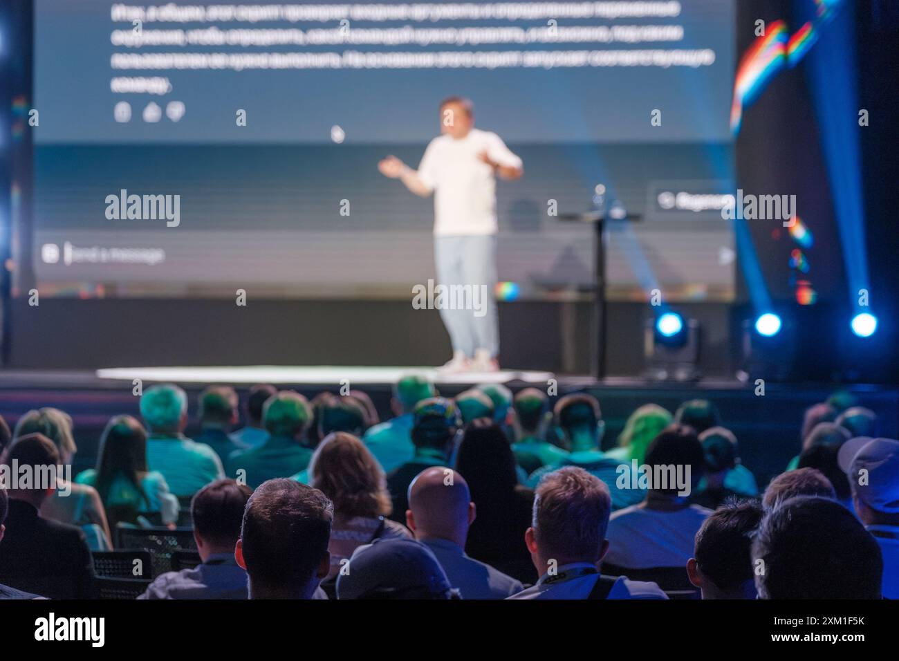 Public speaker giving a presentation on stage to a large audience at a conference. Focus on ...