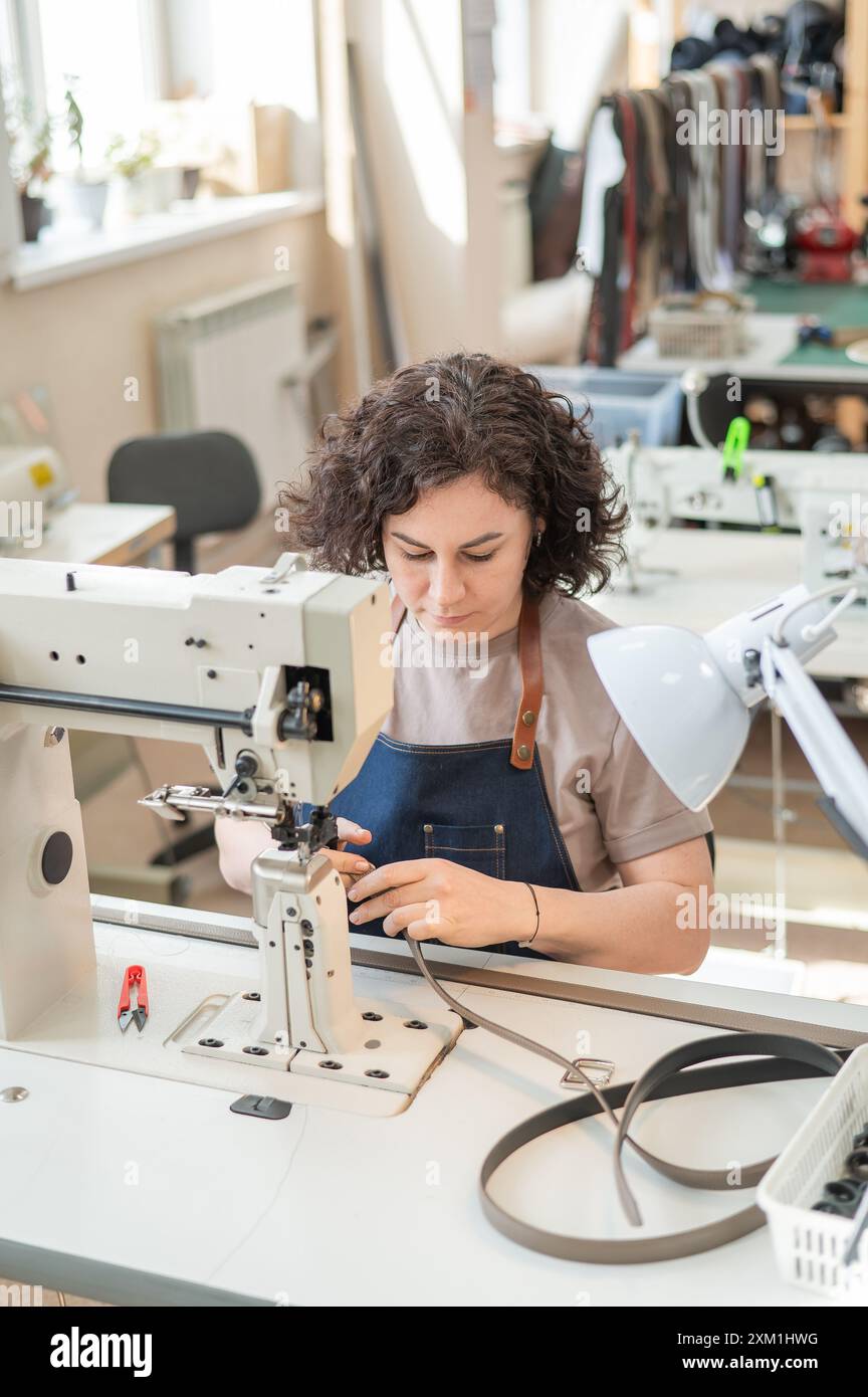 A woman tanner sews a leather belt on a sewing machine. Vertical photo ...