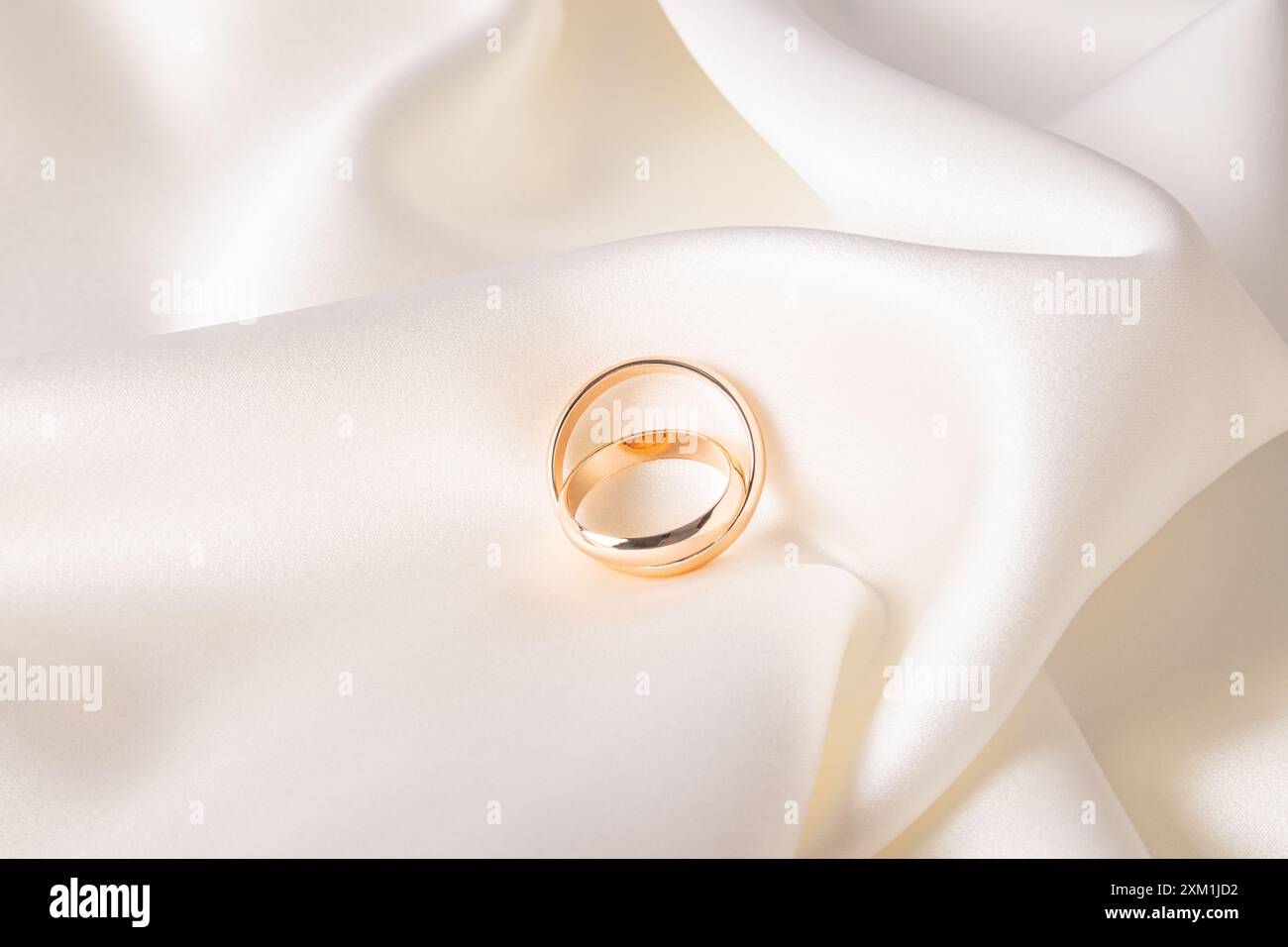 Two gold elegant wedding rings lie on soft folds of beige satin fabric ...