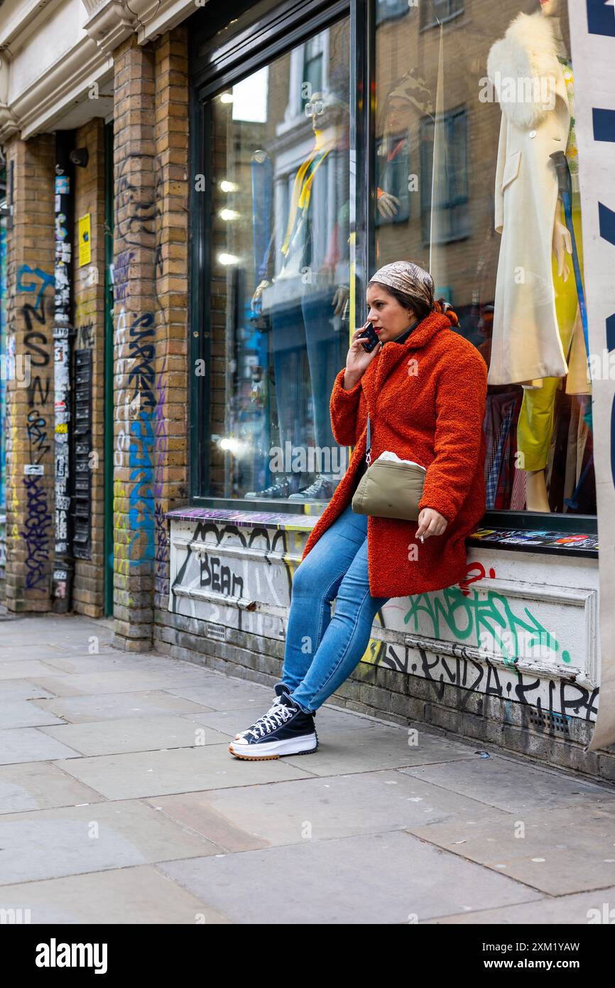 Warmly dressed woman smoking and talking on her cell phone, London ...
