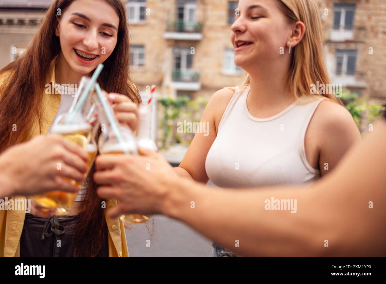 Group of teenagers are having fun and drinking lemonade on street. Cute friends raise toast and ...