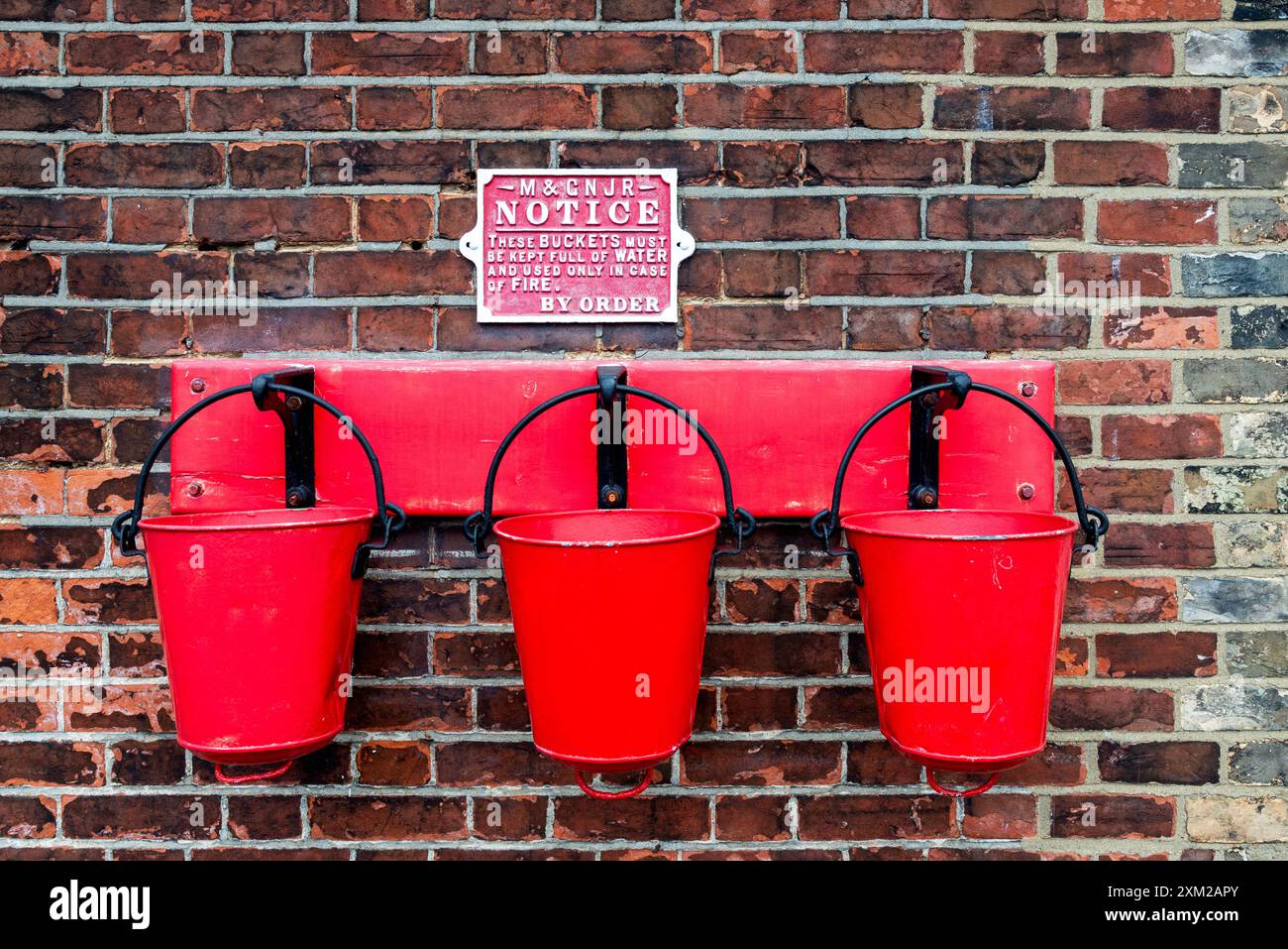 3 vintage fire buckets hanging against a brick wall at Sheringham train ...
