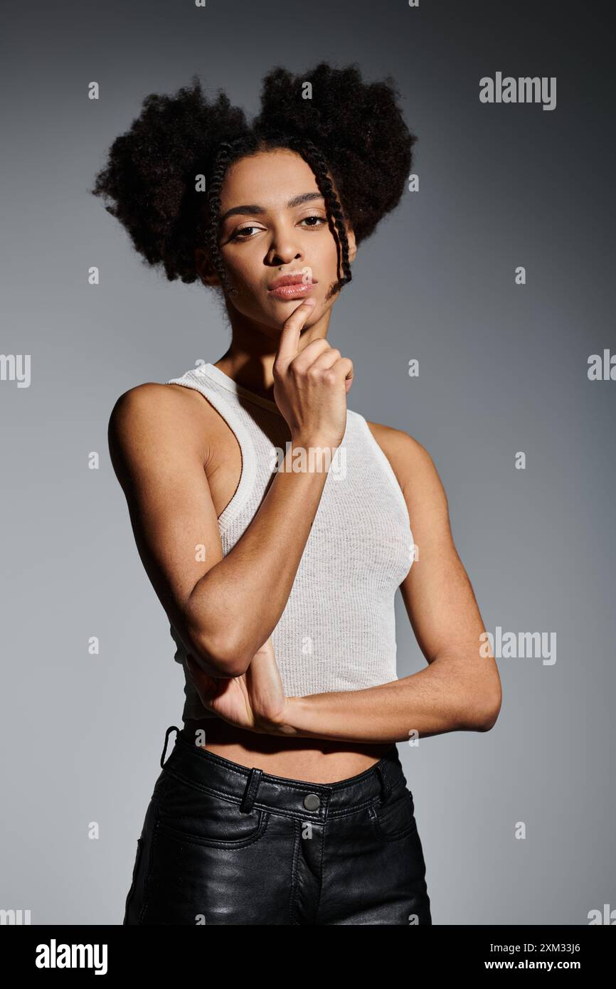 A young African American woman in a white tank top poses against a grey ...