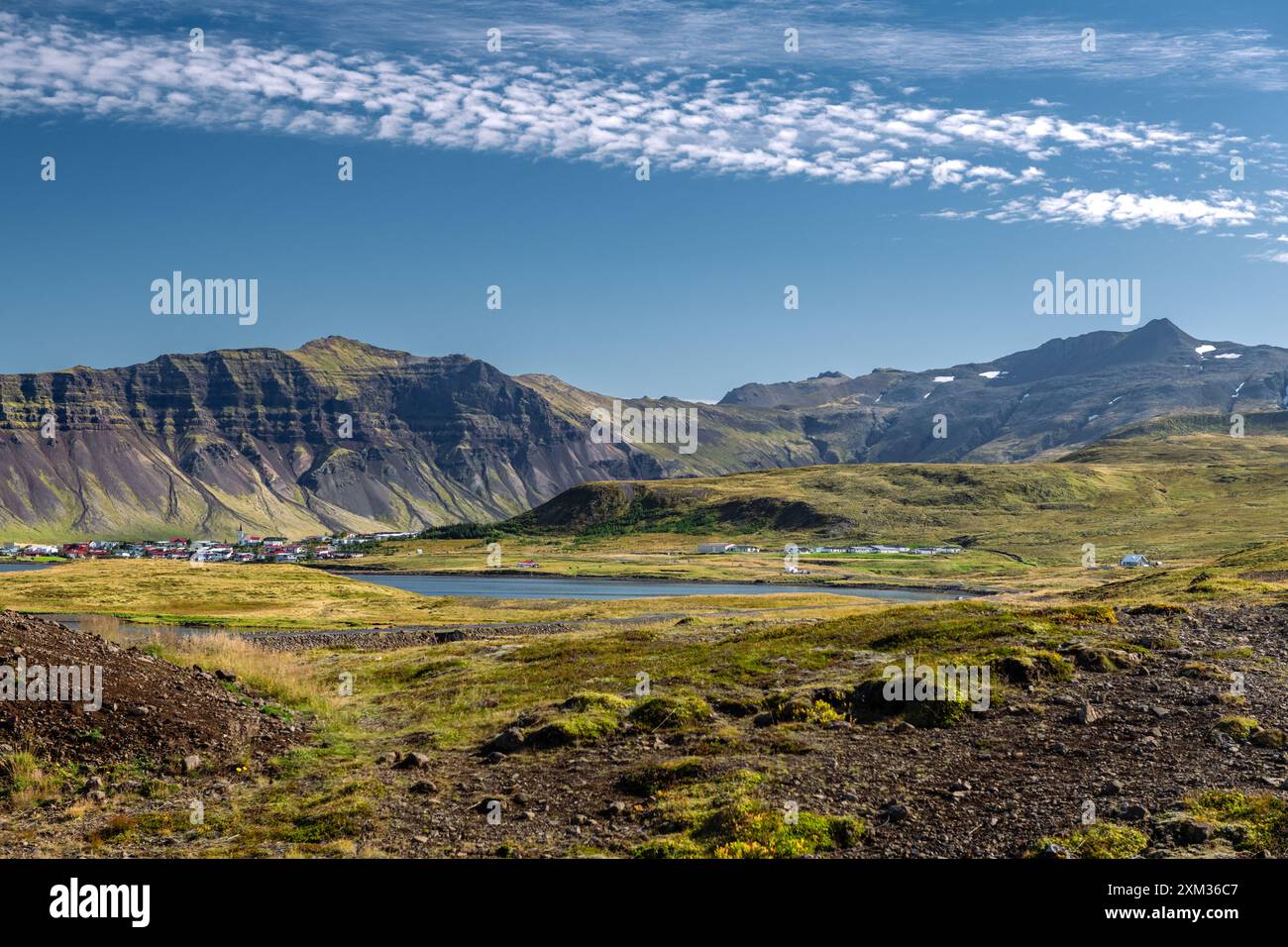 Small village in lush valley with rugged mountains under clear blue sky ...