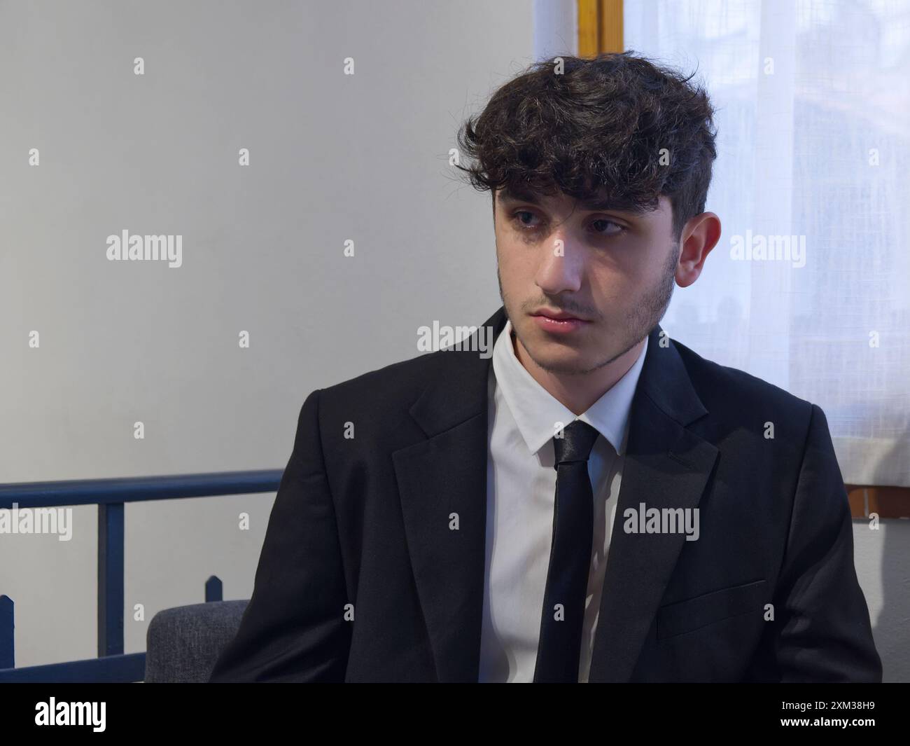 a sitted caucasian teenager in a business suit adjusts his white shirt ...