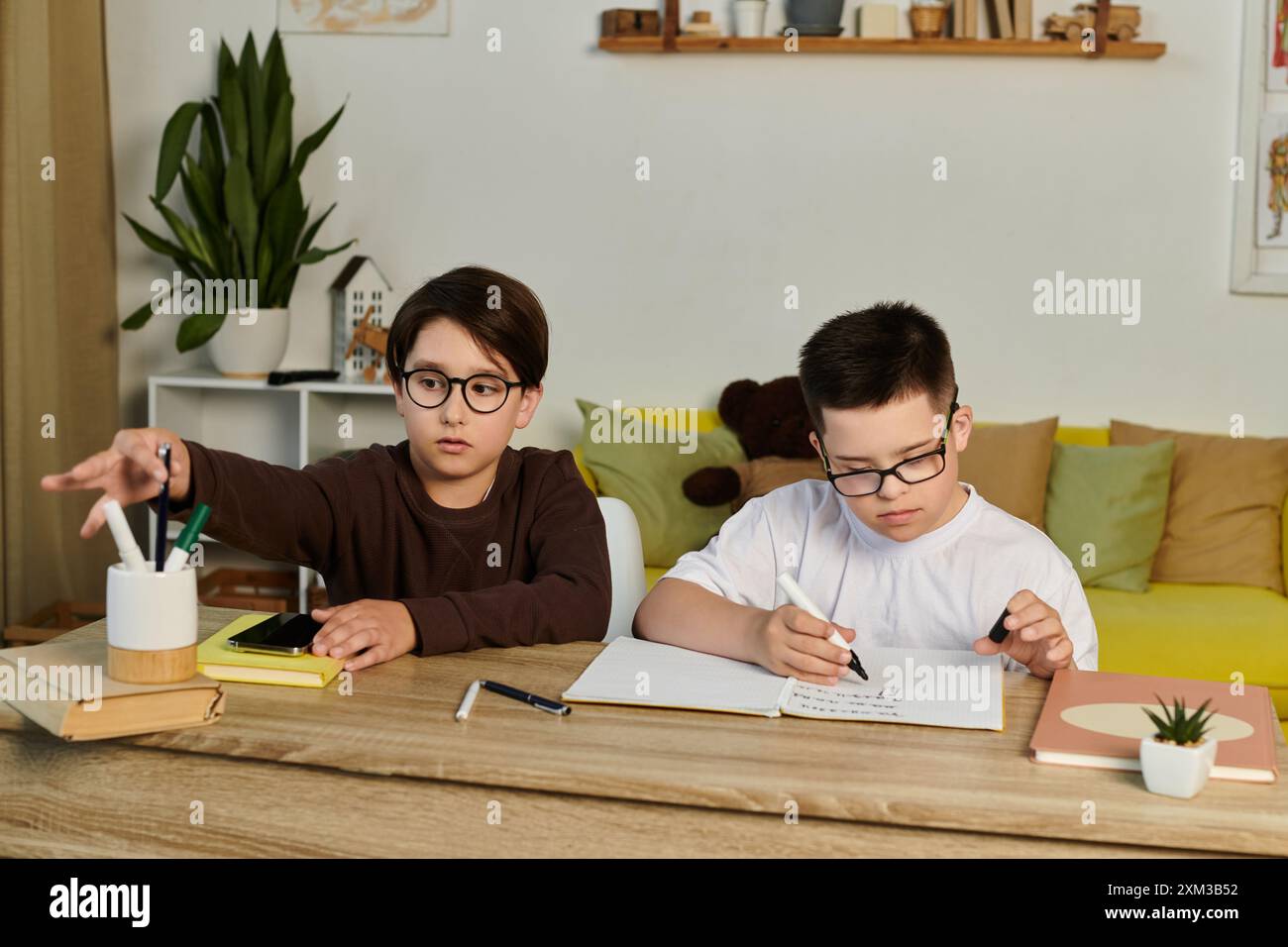 Two young boys, one with Down syndrome, sit at a table doing homework ...