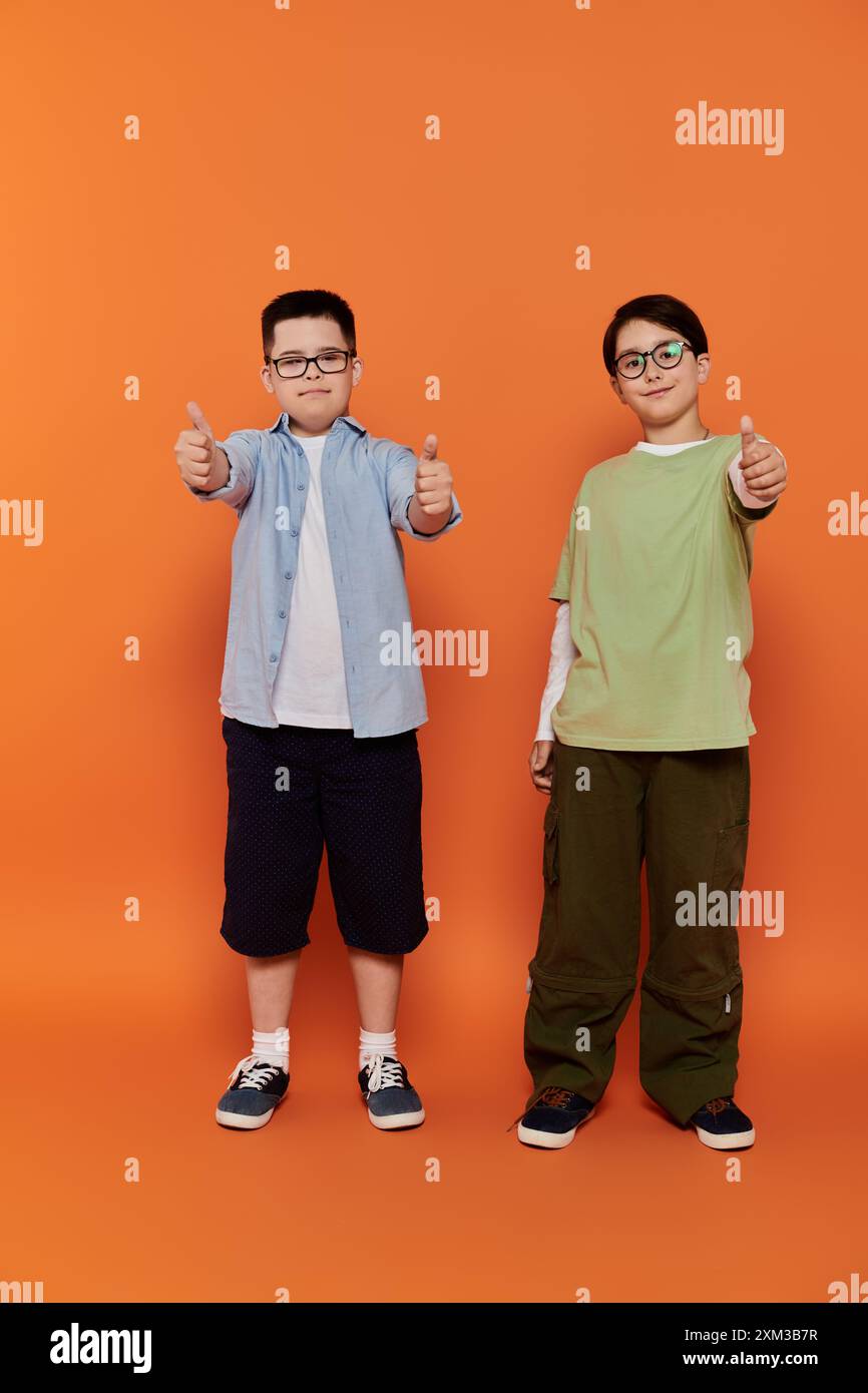 Two boys, one with Down syndrome, stand in a studio and give thumbs up ...