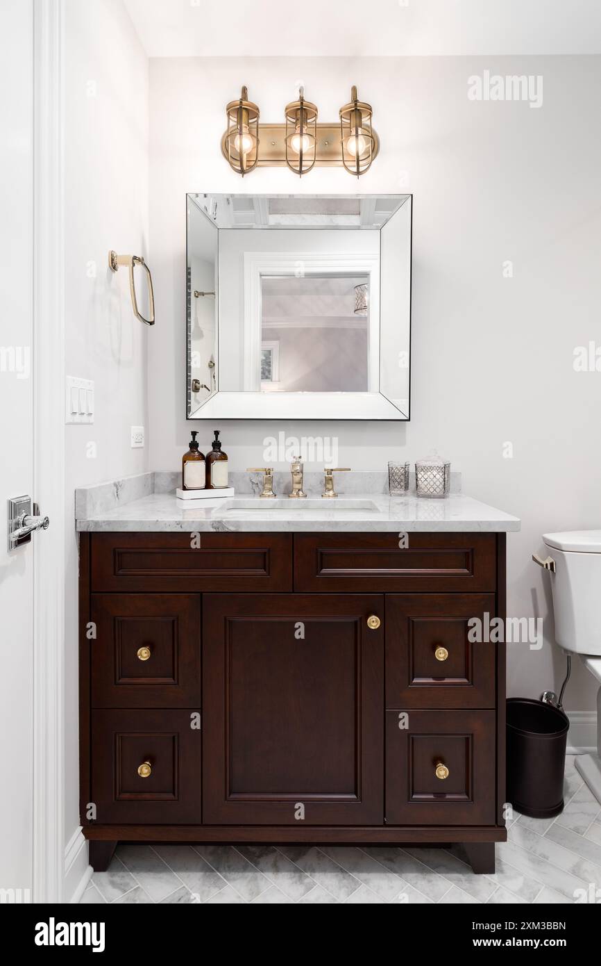 A bathroom with a wooden vanity cabinet, gold light fixture hanging ...