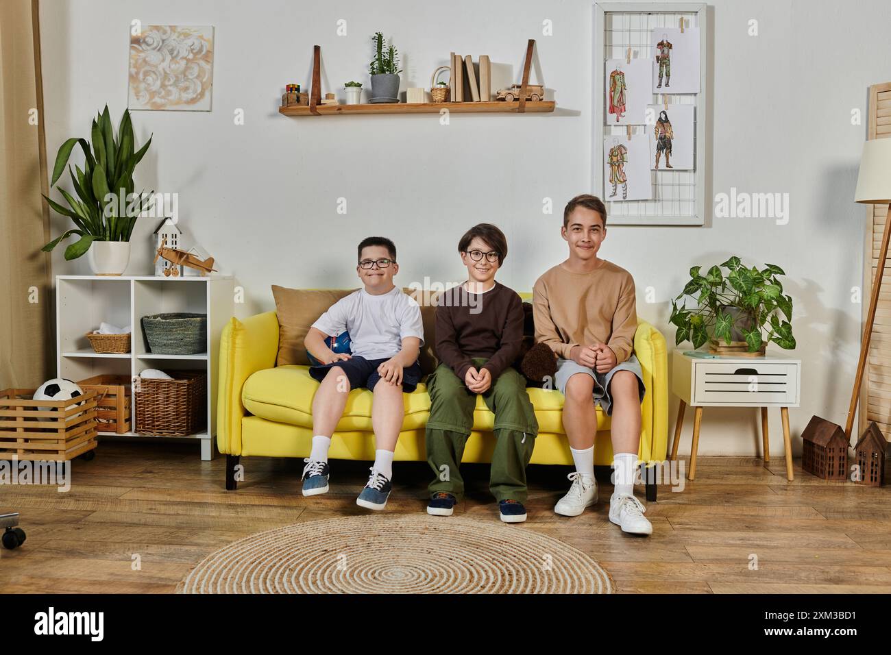 Three young boys sit together on a yellow couch, smiling Stock Photo ...