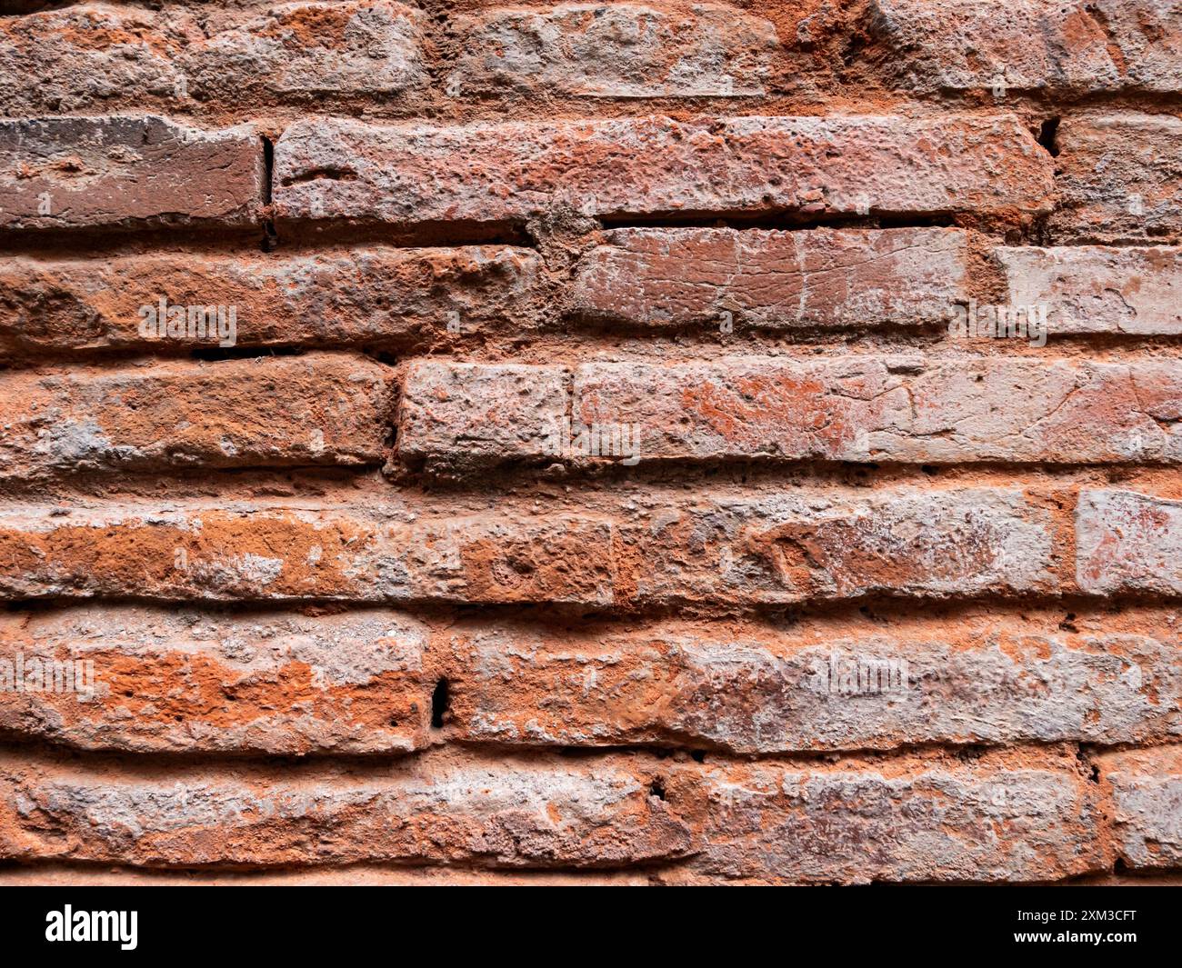 A close-up shot of a weathered red brick wall, featuring rows of bricks ...