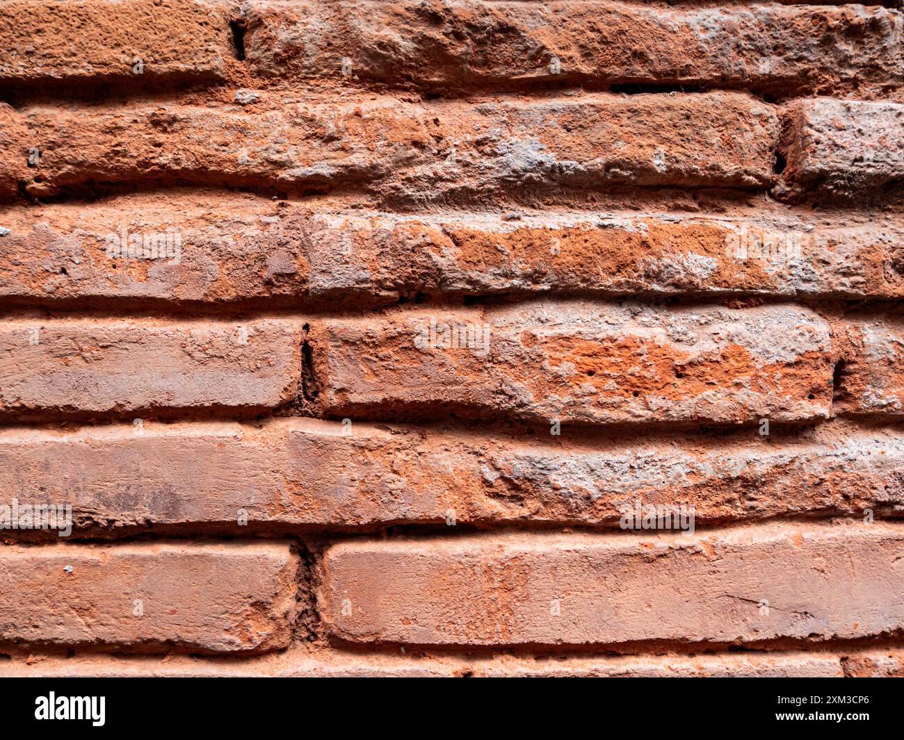 A close-up shot of a weathered red brick wall, featuring rows of bricks ...