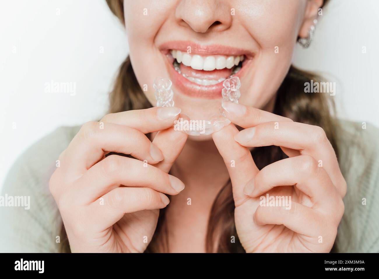 Woman smiling and holding a clear teeth aligner with both hands, dental ...