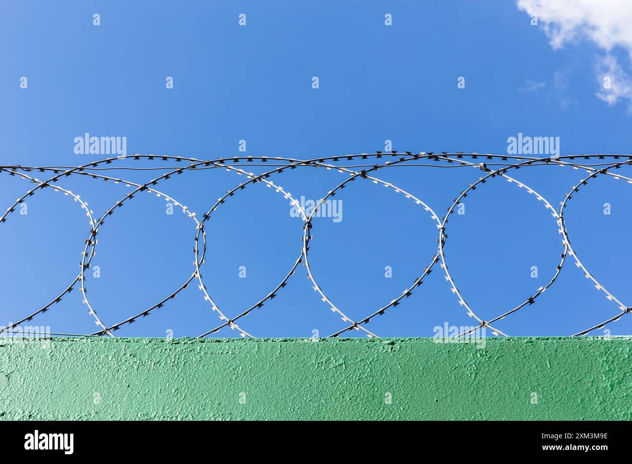 Barbed wire loops atop a green fence under a clear blue sky Stock Photo ...