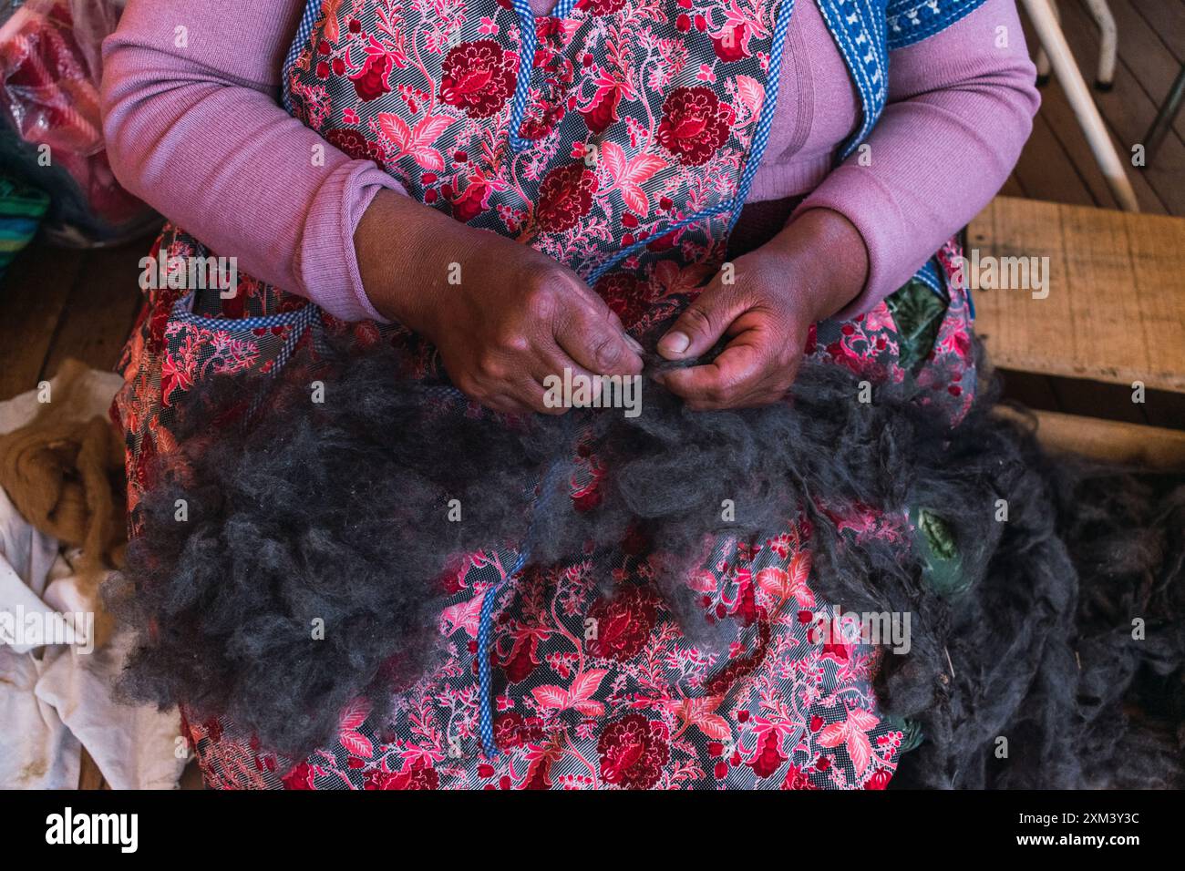 hands of an Andean woman spinning brown alpaca fiber in an ancestral ...
