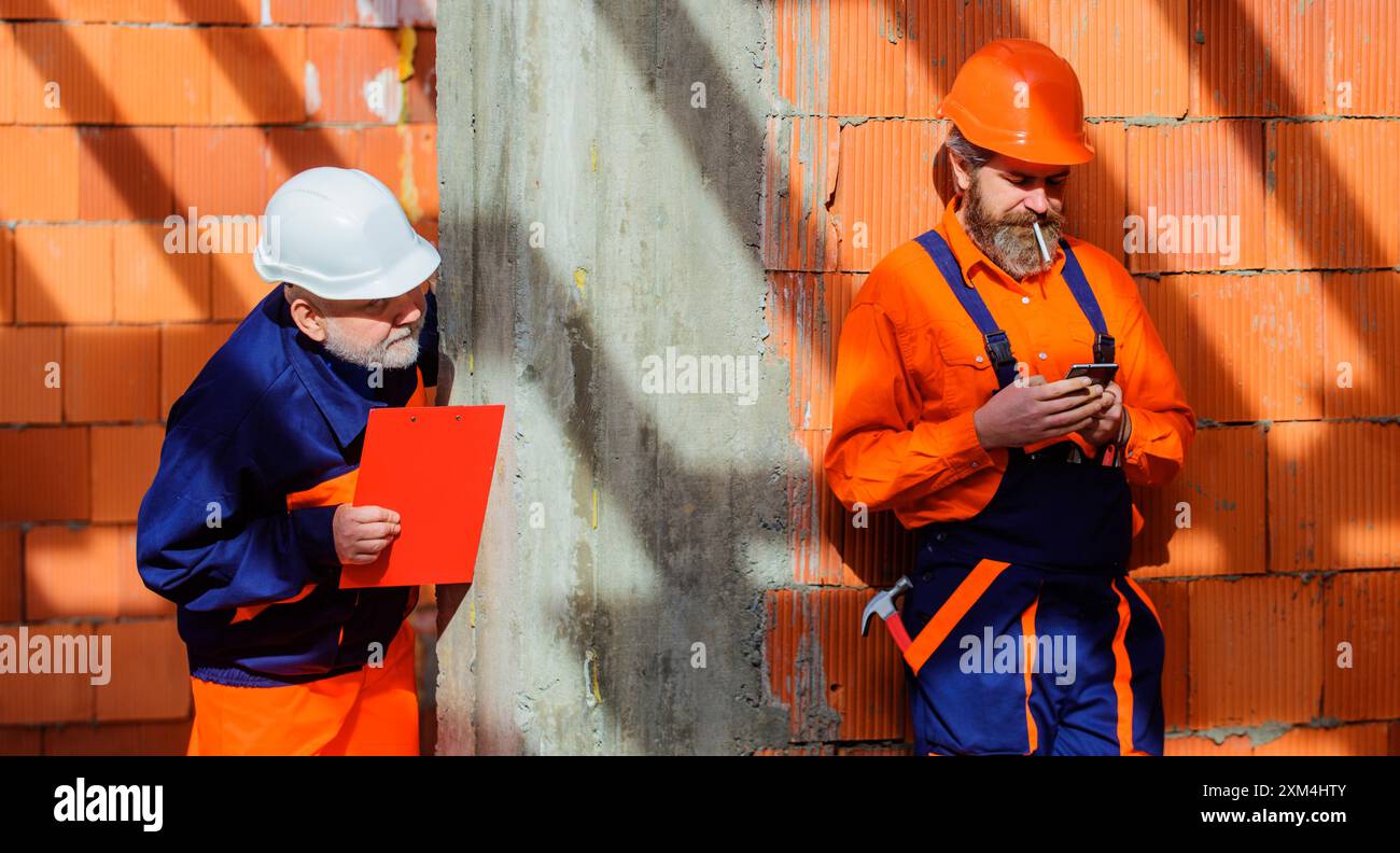 Two builders in hard hat on construction site. Male builder in uniform ...