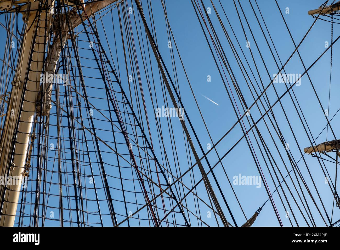 Nautical rigging on tall ship under clear sky with airplane contrail ...