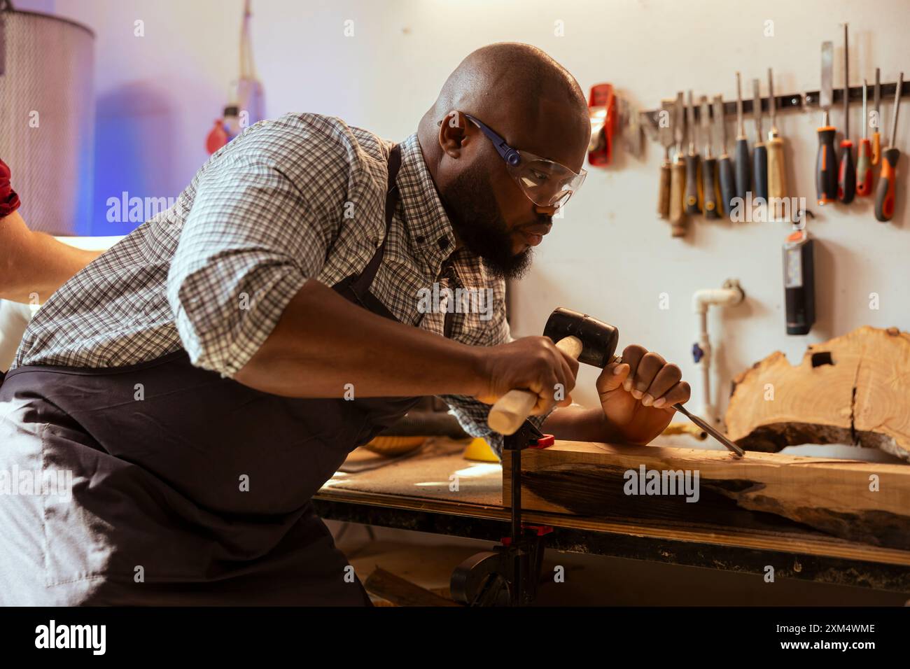 BIPOC man in carpentry shop wearing protection equipment while carving ...