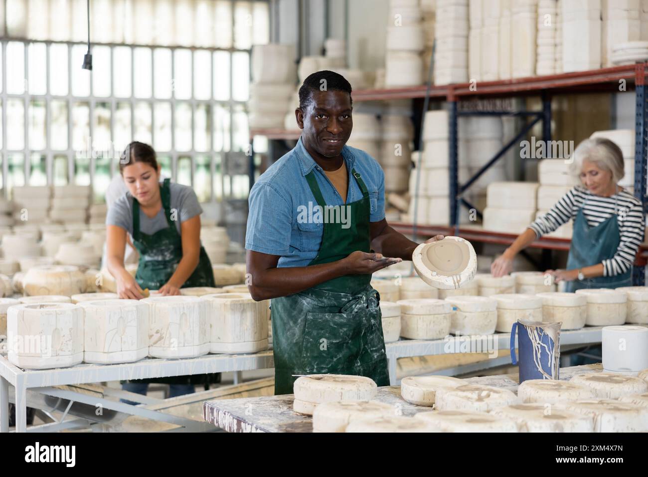 African american worker pours slip clay mass from jug into plaster mold ...