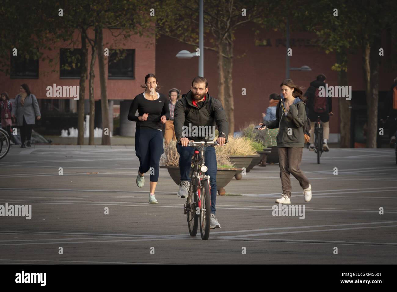 This photo depicts a man cycling in the foreground while others jog and ...