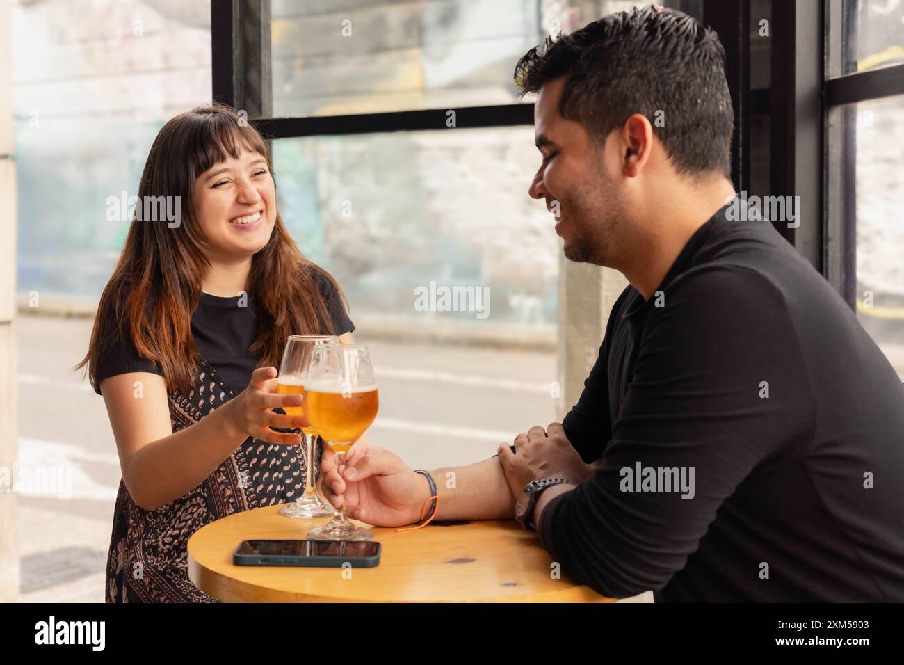Man and woman drinking beer in a bar during the day, laughing and ...