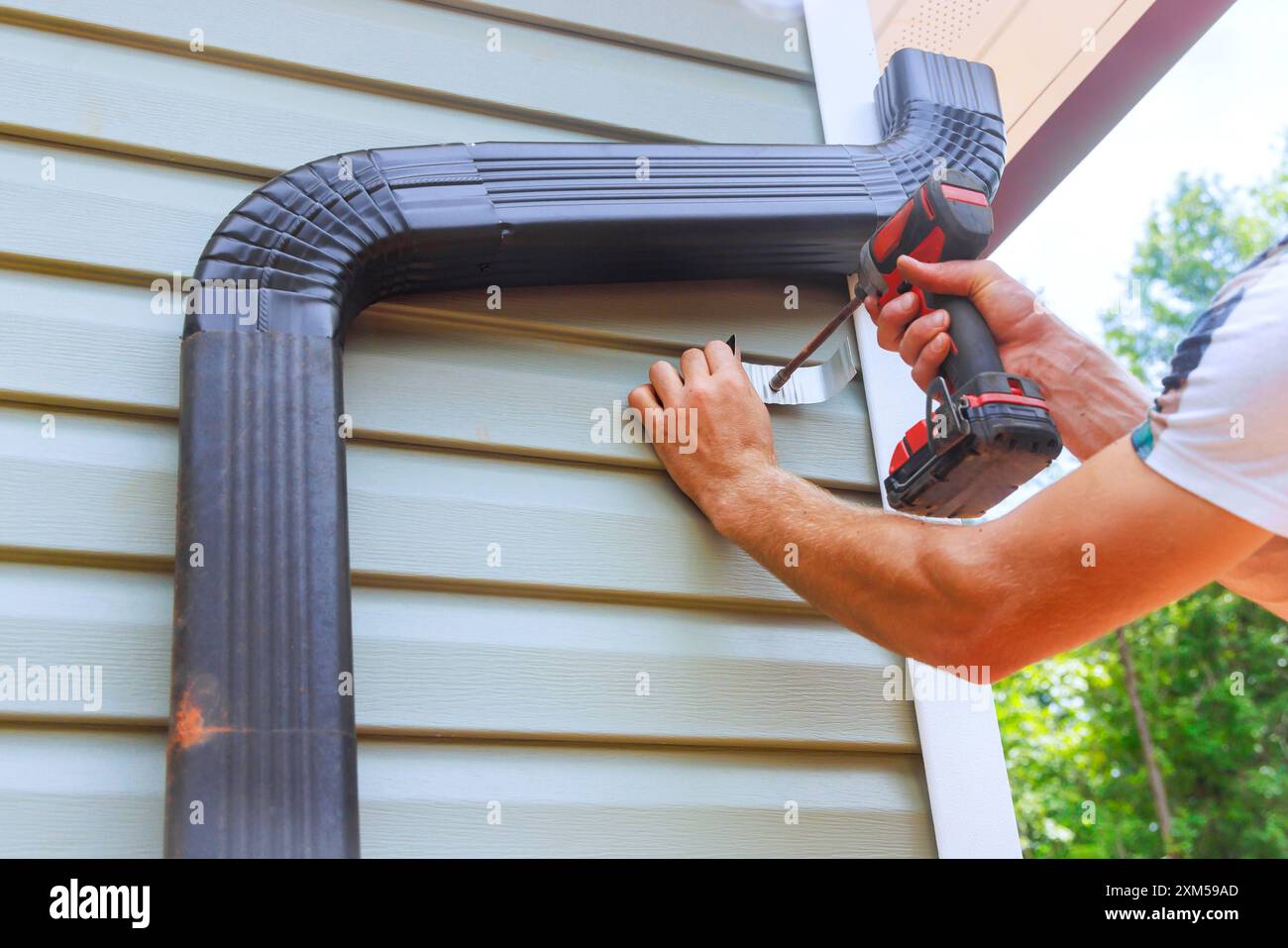 Worker installing rain gutters on roof, fitting downpipes, installing ...