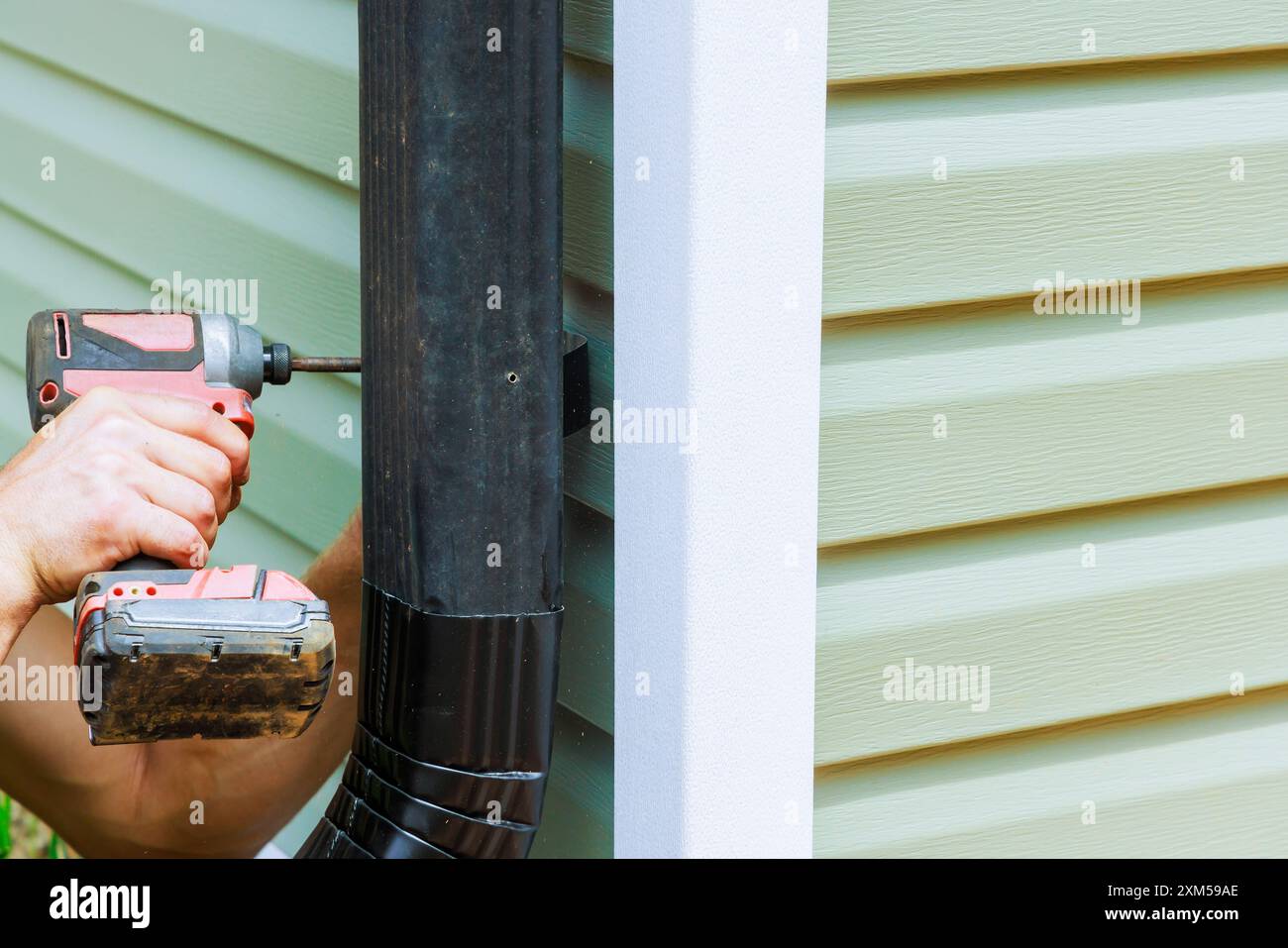 Worker installing rain gutters on roof installing downpipes downspout ...