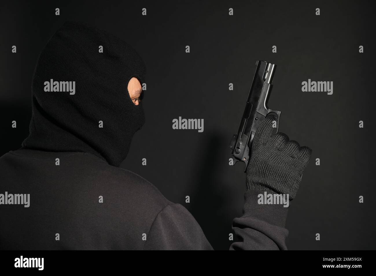 Dangerous masked criminal with gun on black background. Armed robbery ...
