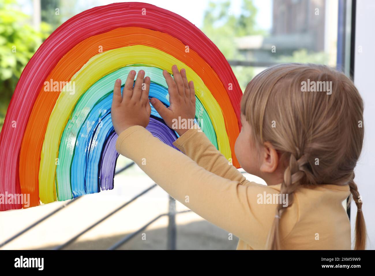 Little girl touching picture of rainbow on window indoors Stock Photo ...