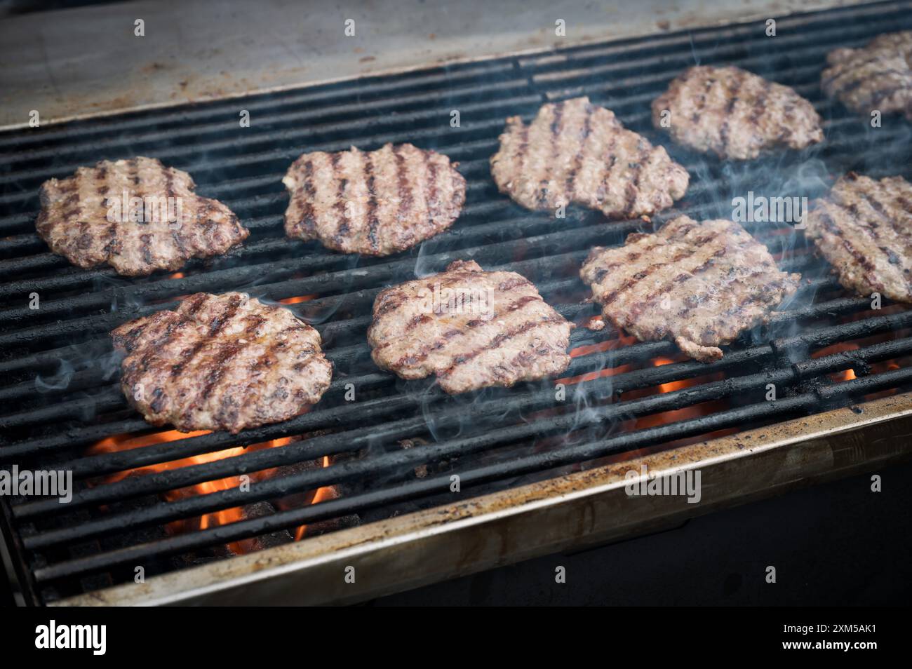 Hamburger patties cook on an open flame grill at a take out restaurant ...