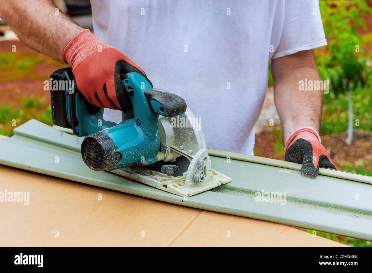 Working with circular handsaw, worker cuts plastic vinyl siding to ...