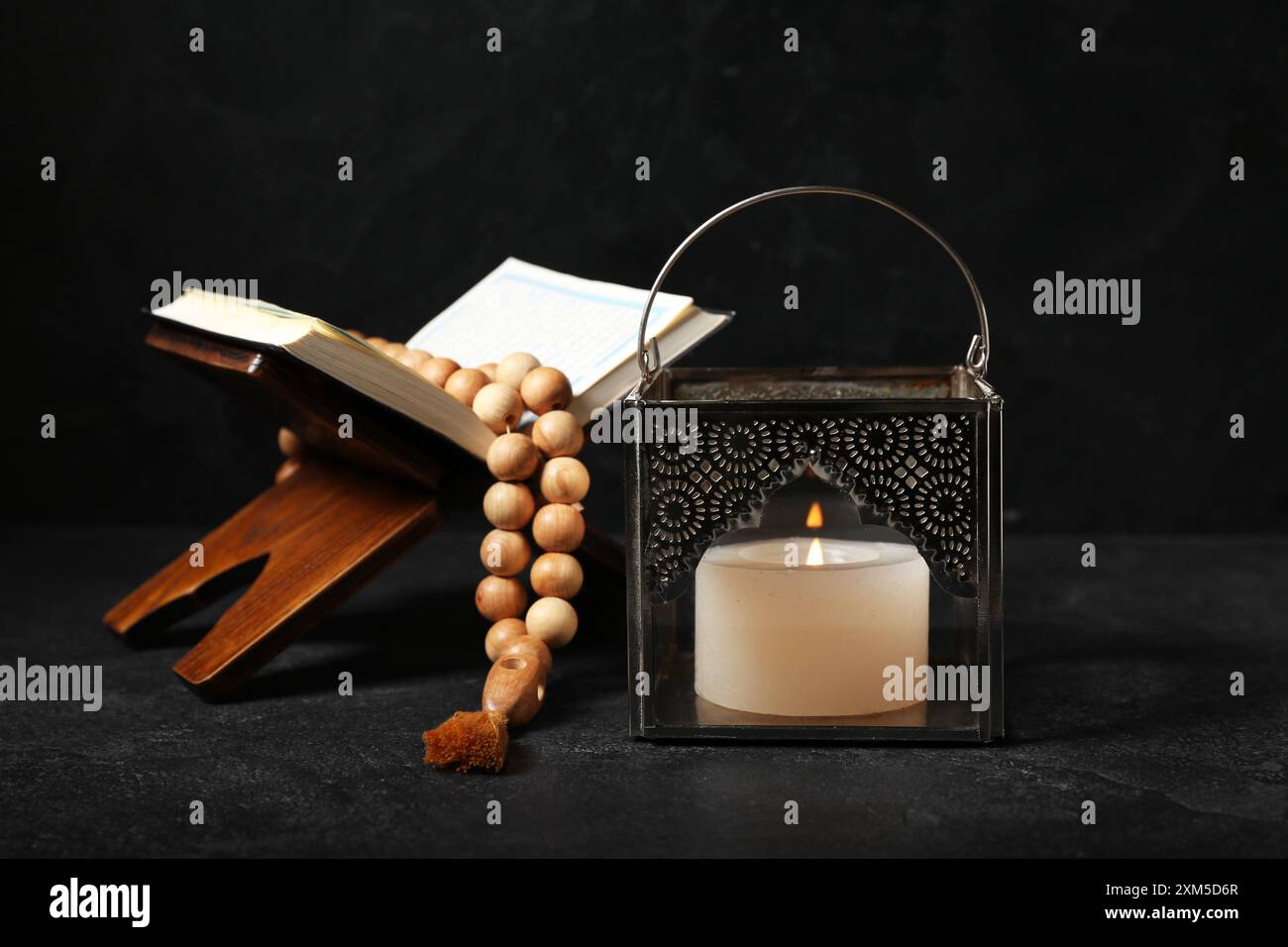 Muslim lamp with burning candle, Koran and prayer beads on dark ...