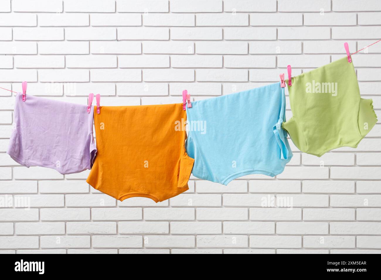 Clean clothes hanging on rope against light brick wall Stock Photo - Alamy