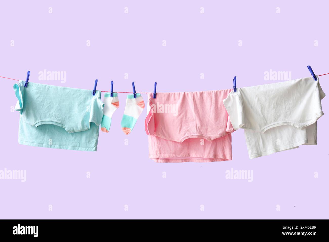 Clean clothes hanging on rope against lilac background Stock Photo - Alamy