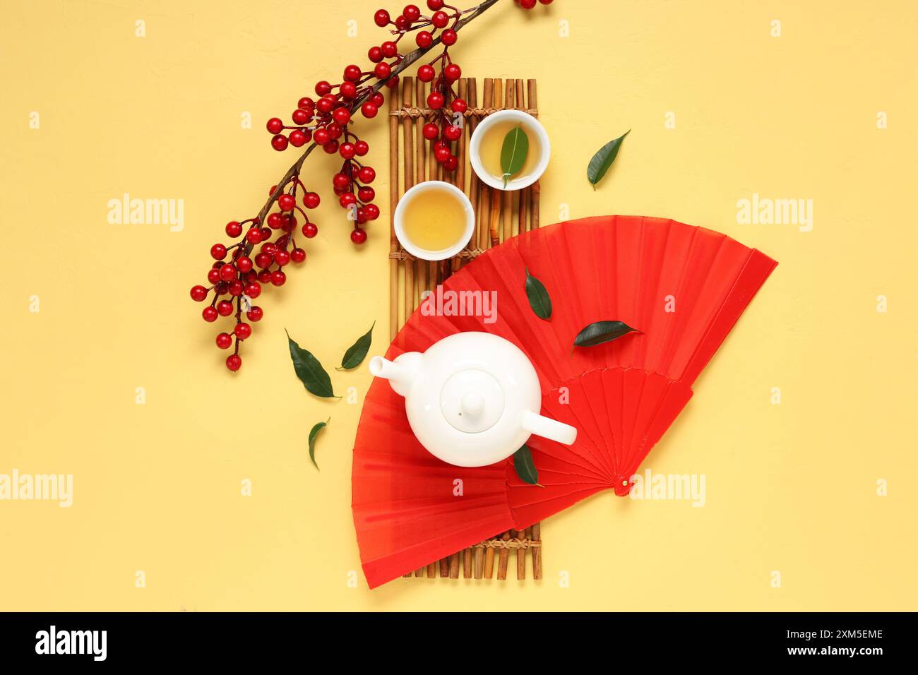 Teapot with cups of tea, fan and viburnum branch on yellow background ...