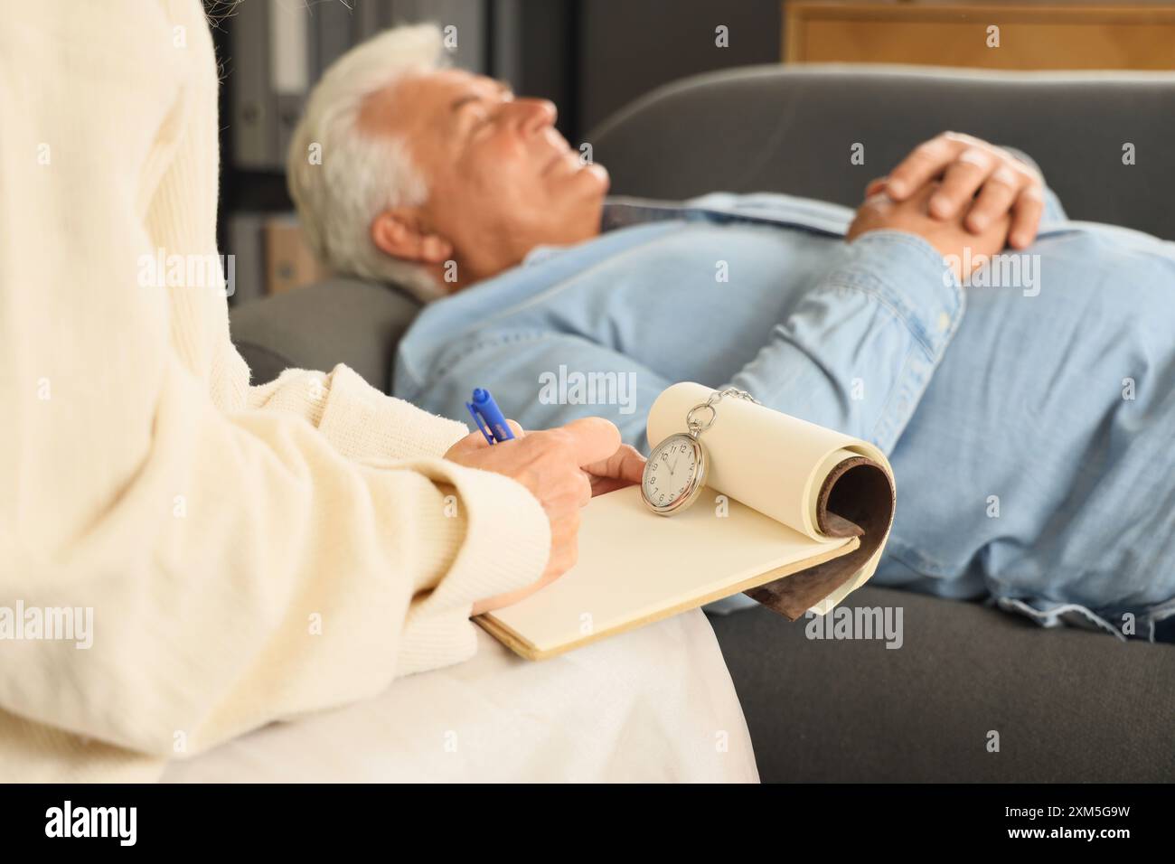 Female hypnotist with pocket watch writing in notebook at office ...