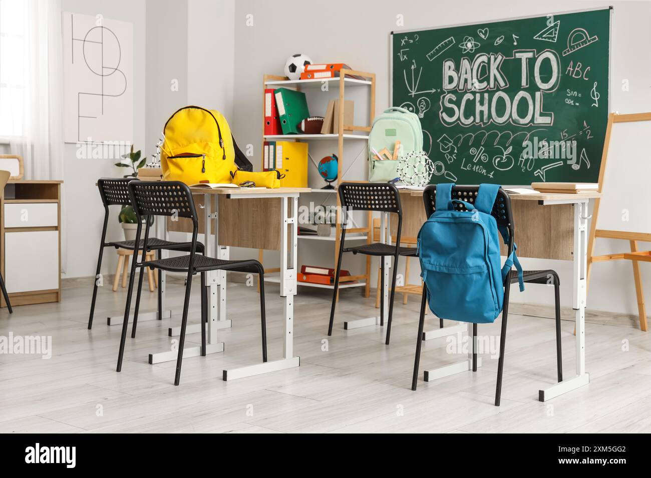 School desks, backpacks and blackboard in light classroom Stock Photo ...