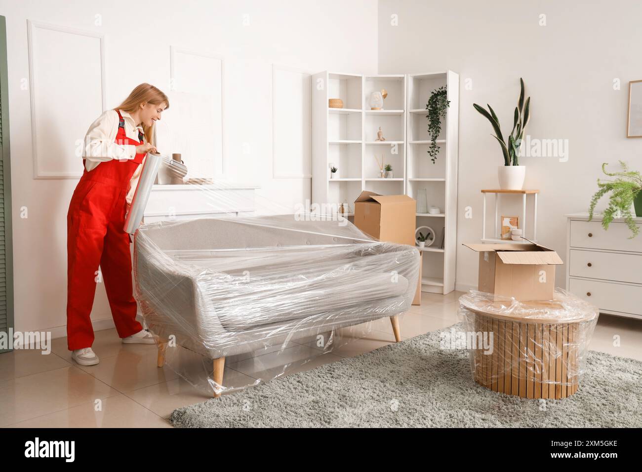 Female worker wrapping sofa with stretch film in room Stock Photo - Alamy