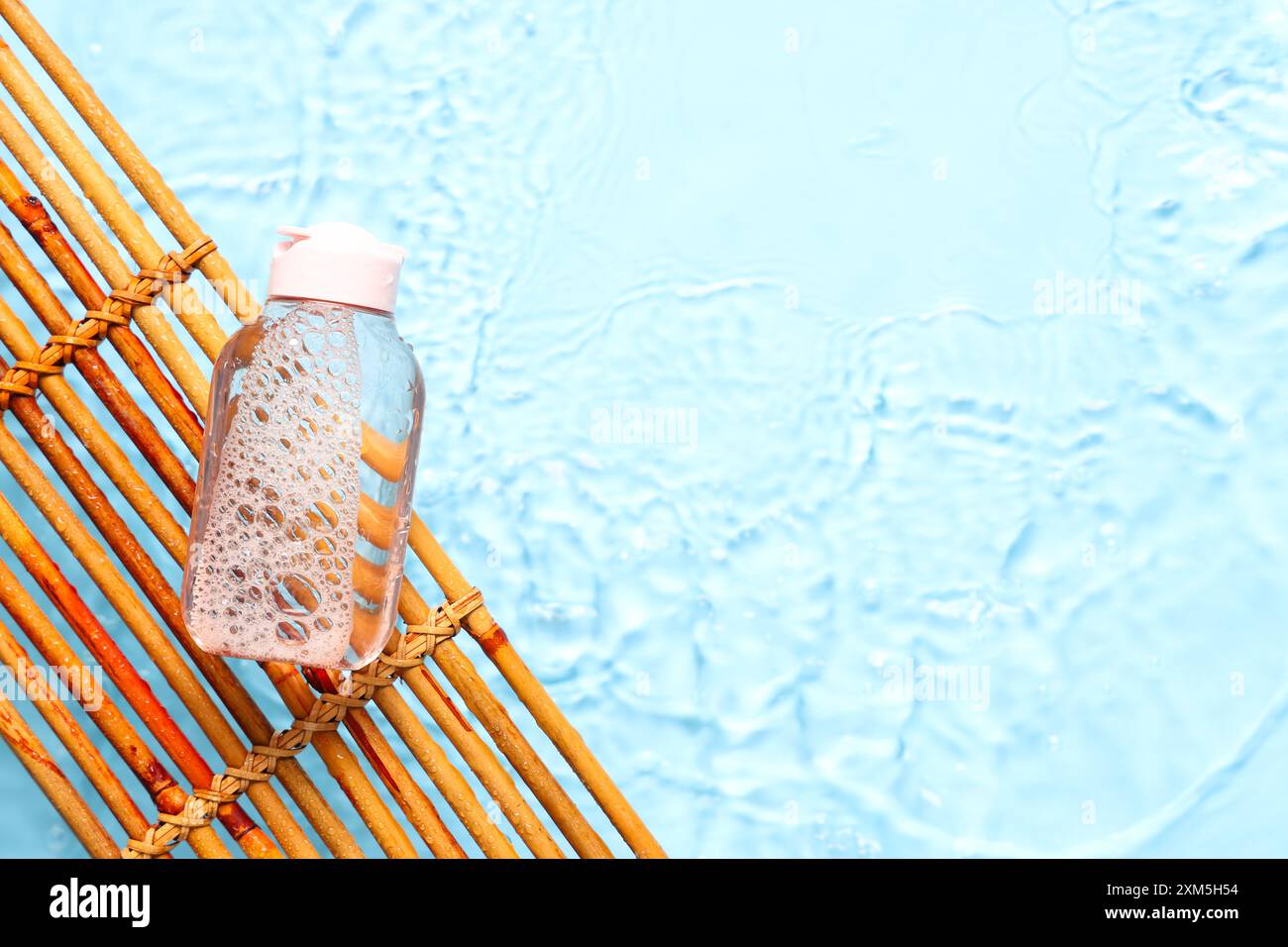 Bottle of micellar water and wicker tray on wet blue background ...